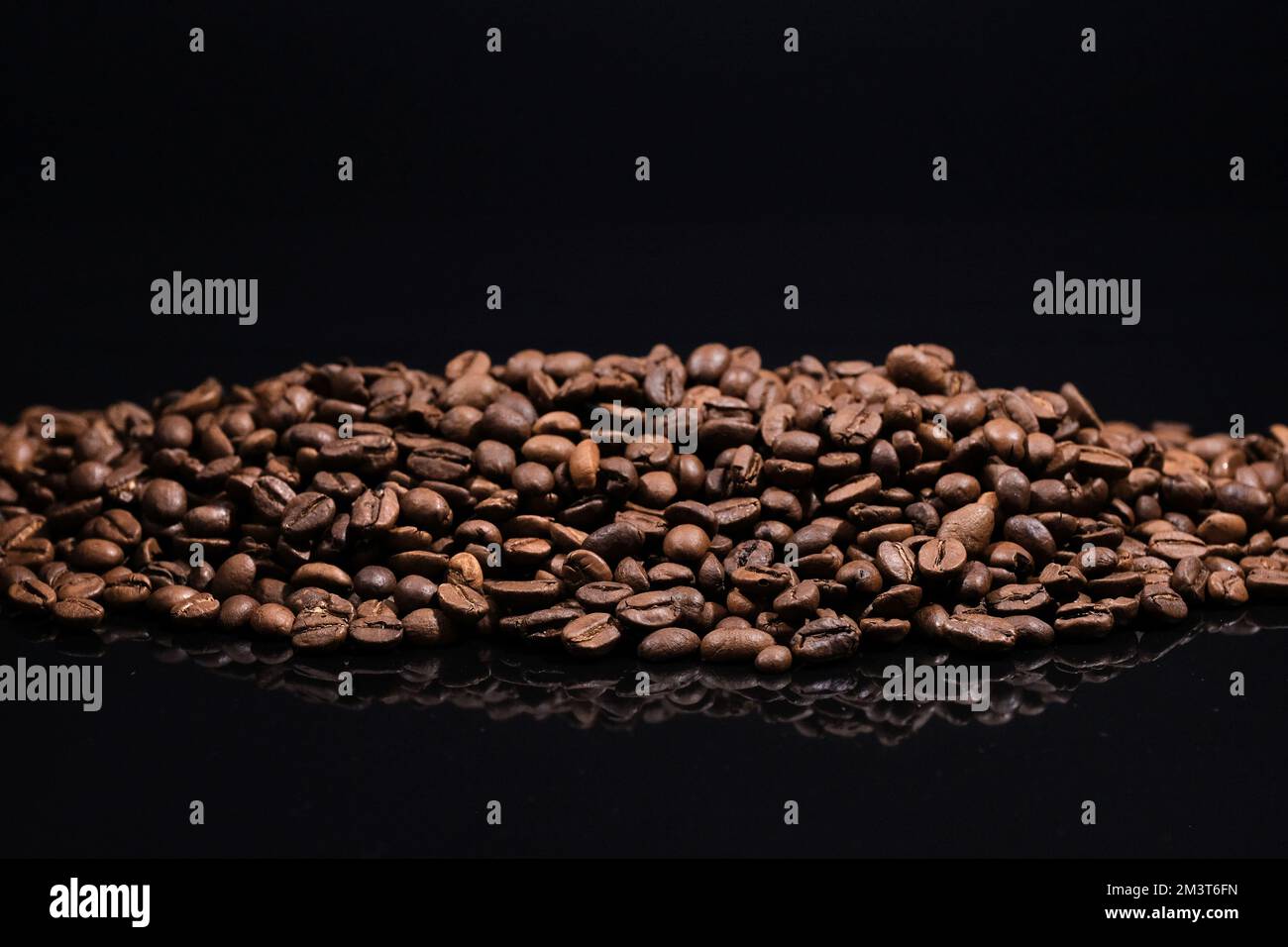 A pile of roasted coffee on a black background with reflection. The ...