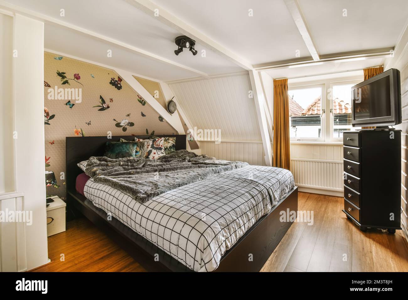 a bedroom with a bed, dressers and tv in the corner on the wall above ...