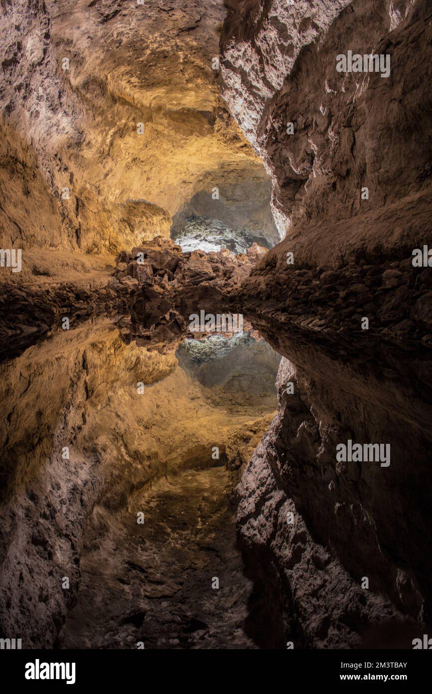 A vertical shot of a hidden cave with still water reflecting the cave ...