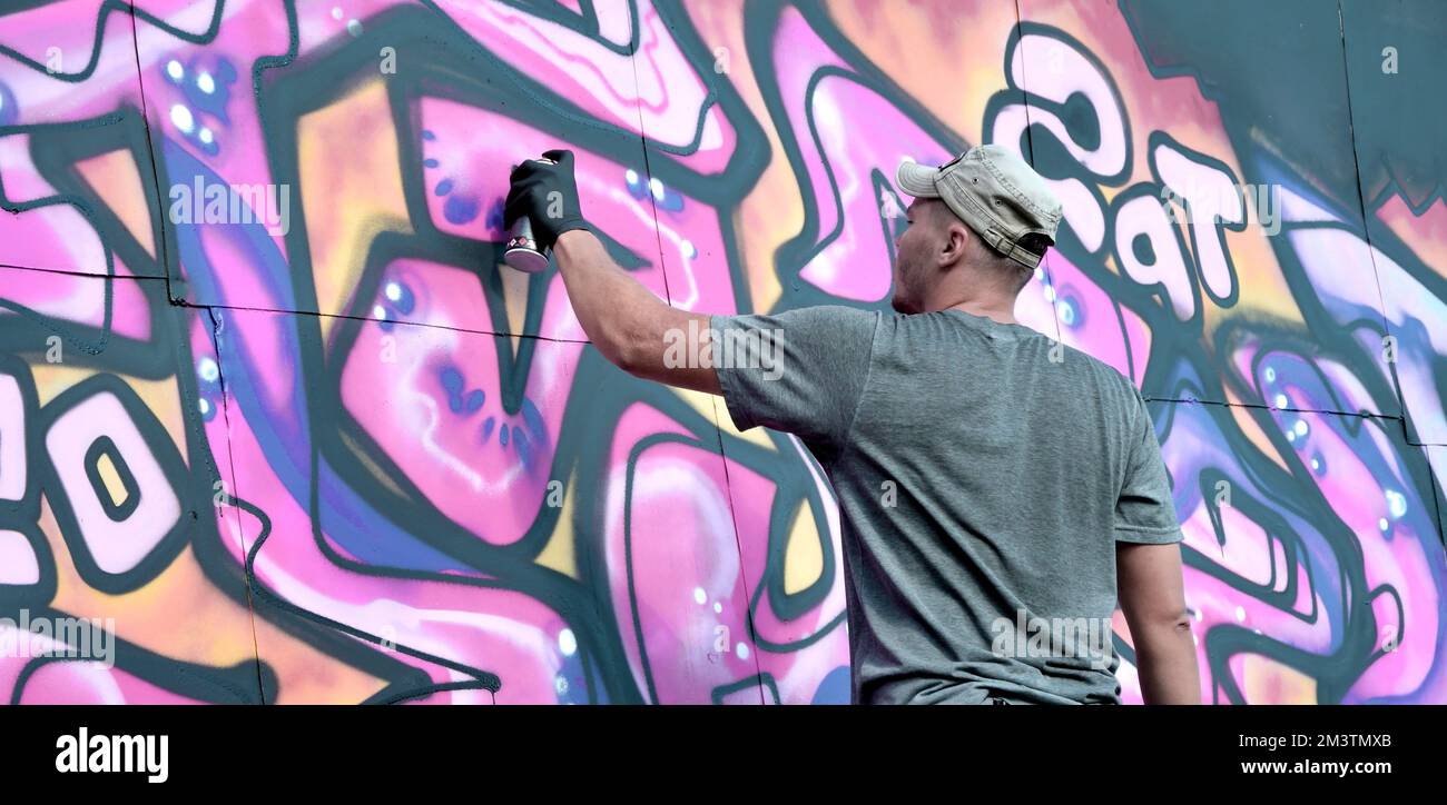 Young caucasian male graffiti artist drawing big street art painting in ...
