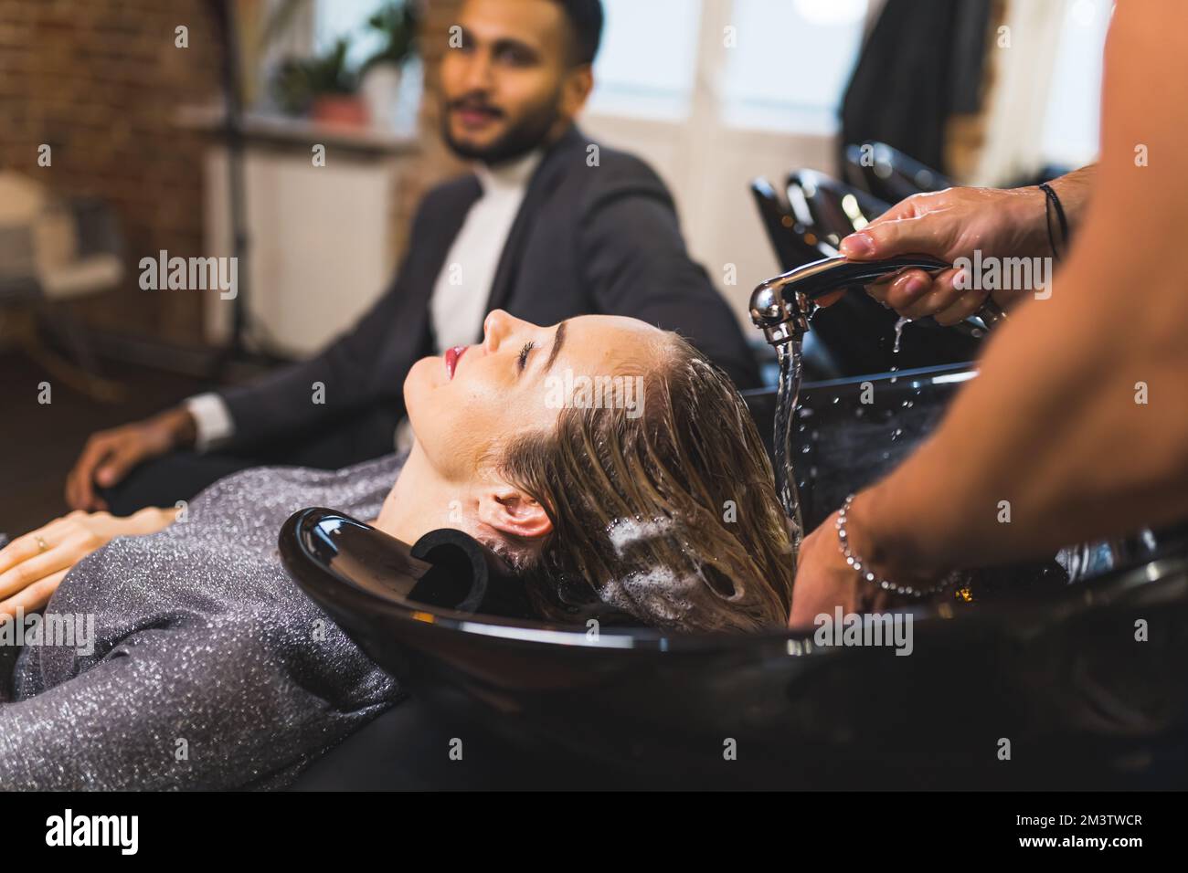 Hairdresser rinsing hair of female customer with water after using ...