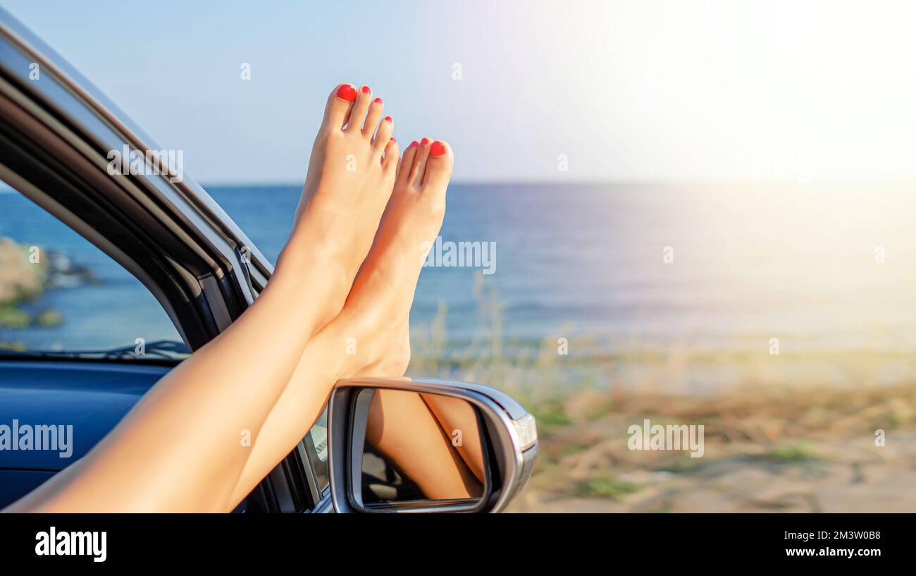 Female legs out of a car window on a background of a sea landscape ...
