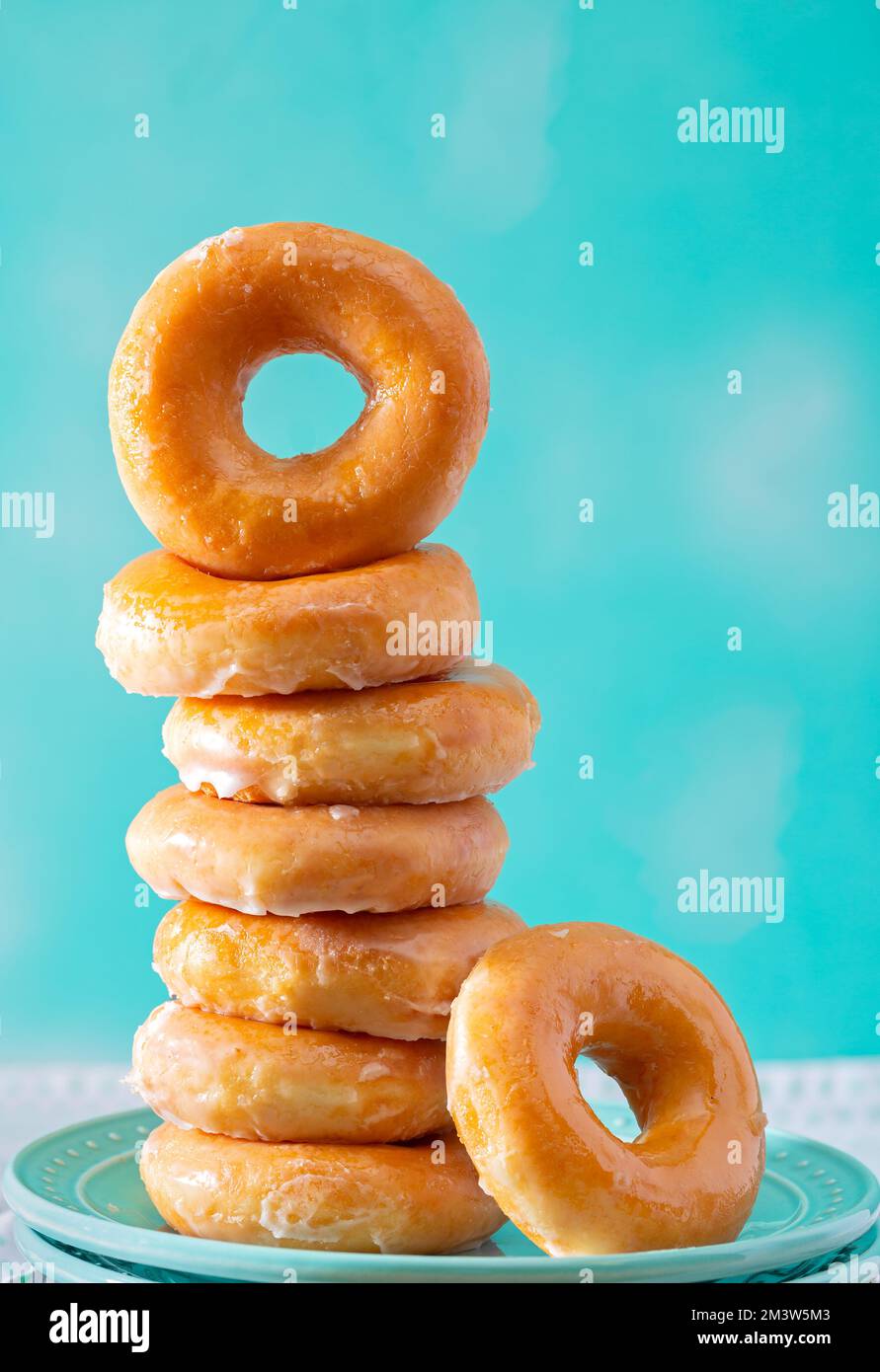 Tall stack of plain glazed doughnuts on a turquoise colored background ...