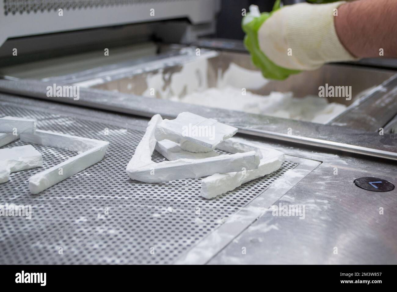 Male worker taking out models from white polyamide powder in working ...