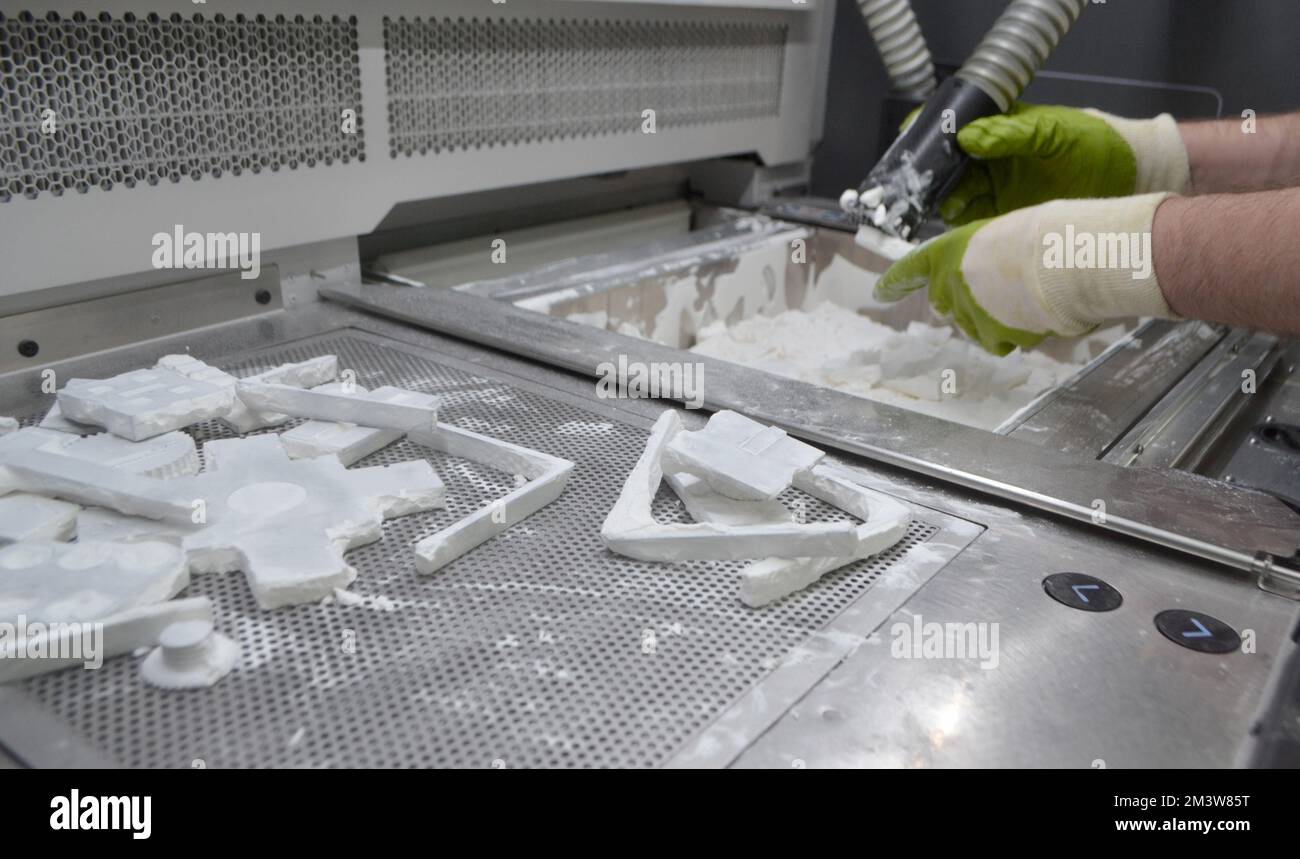 Male worker taking out models from white polyamide powder in working ...