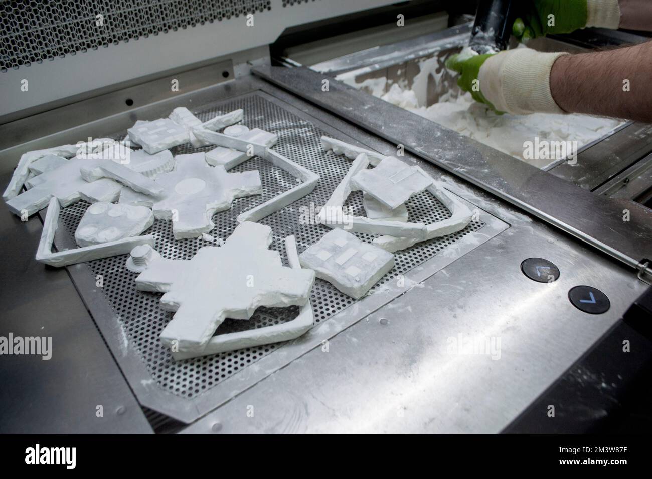 Male worker taking out models from white polyamide powder in working ...