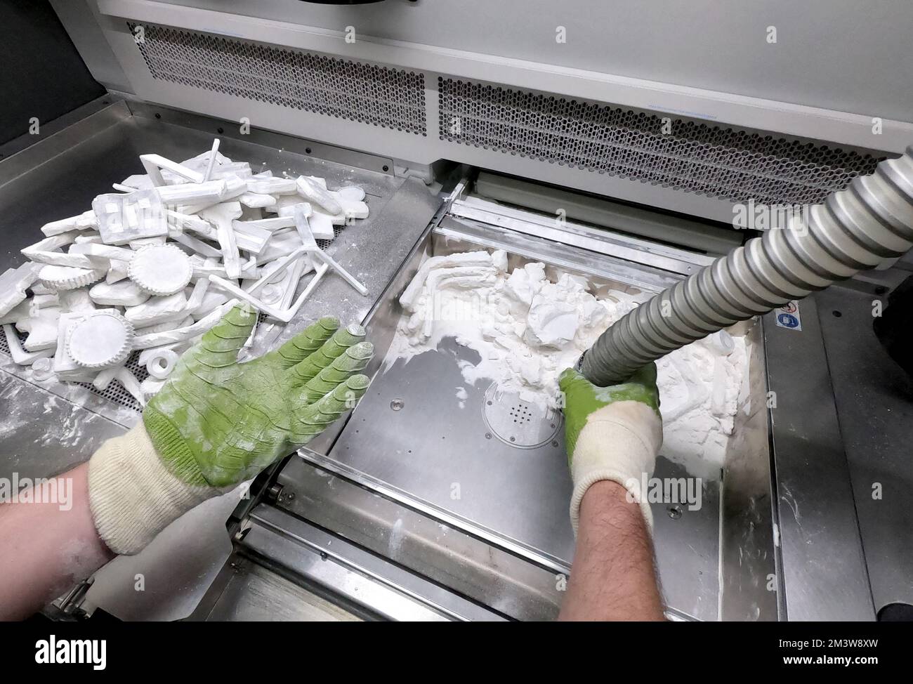 Male worker taking out models from white polyamide powder in working ...