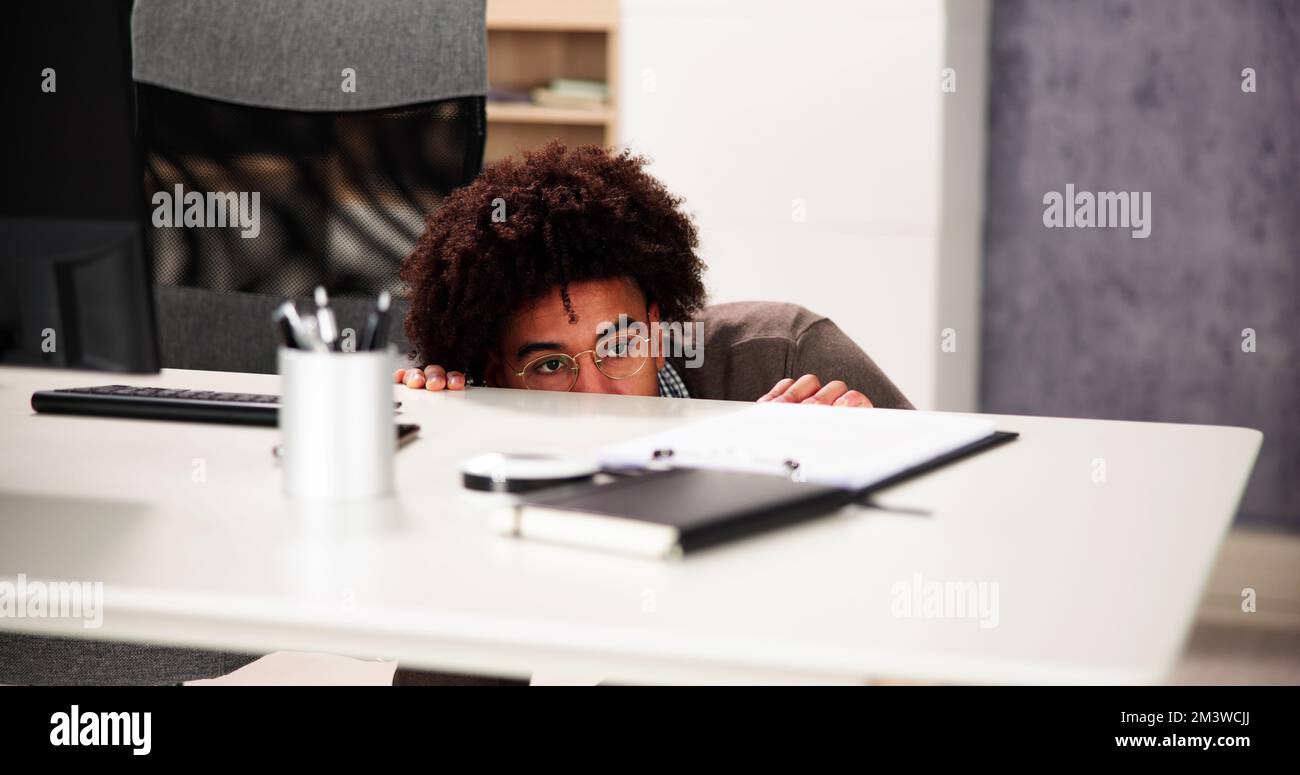Scared Man Hiding Behind Office Desk In Room Stock Photo - Alamy