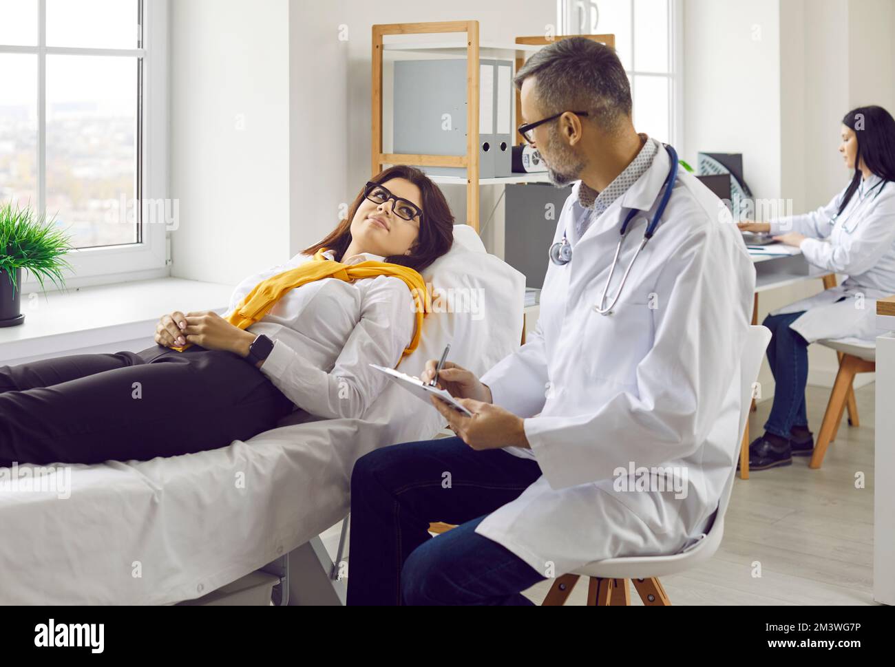 Patient lies on examination couch and listens to her doctor, who makes ...