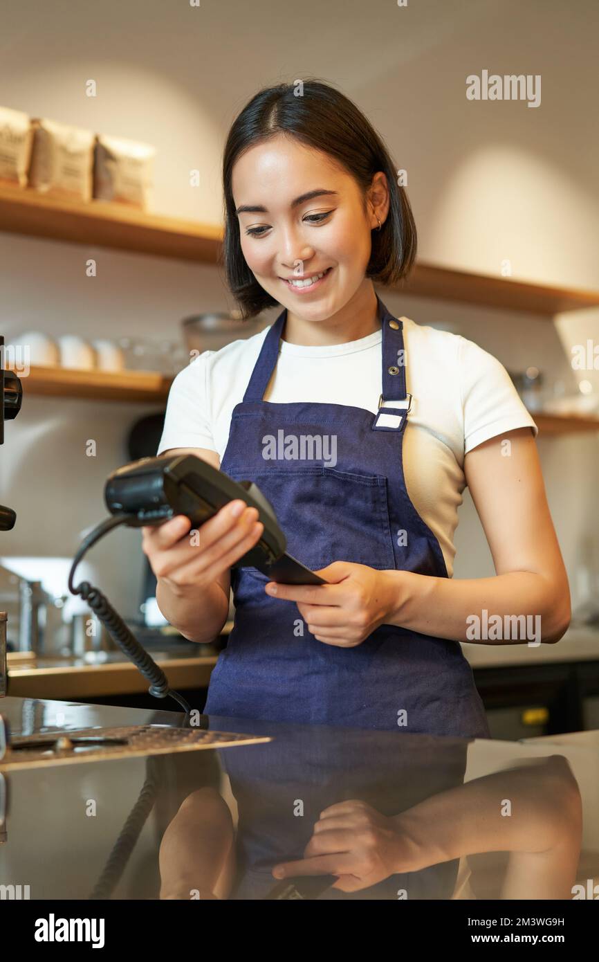 Beautiful smiling asian girl, barista insert client credit card in POS ...