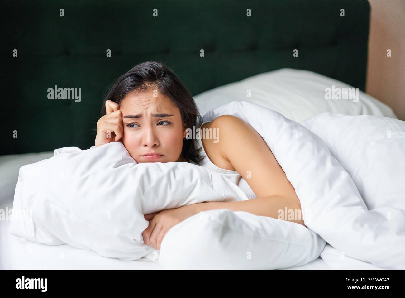 Sad and gloomy asian girl lying in her bed, grimacing and crying ...