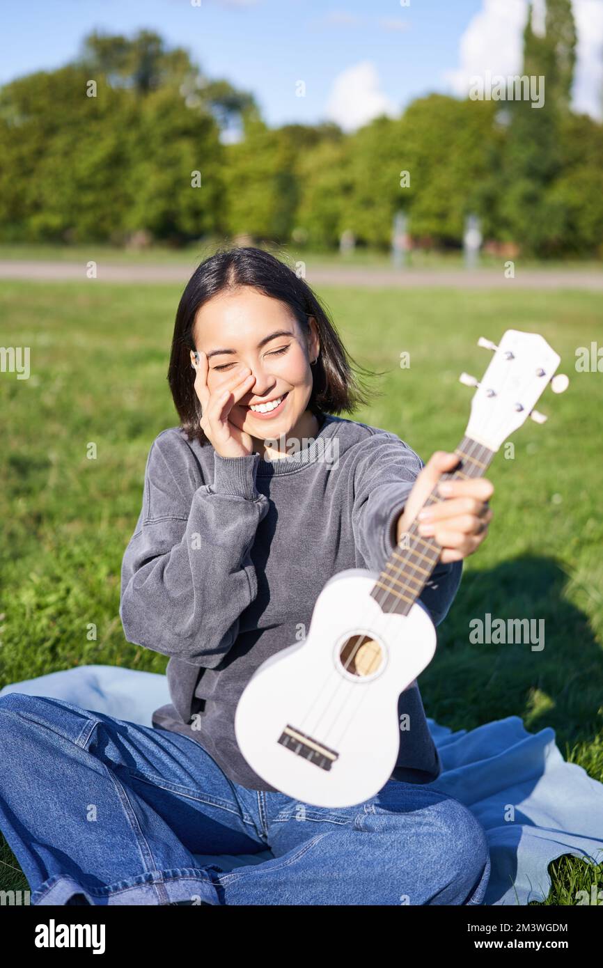 Music and instruments. Smiling asian girl shows her white ukulele, sits ...