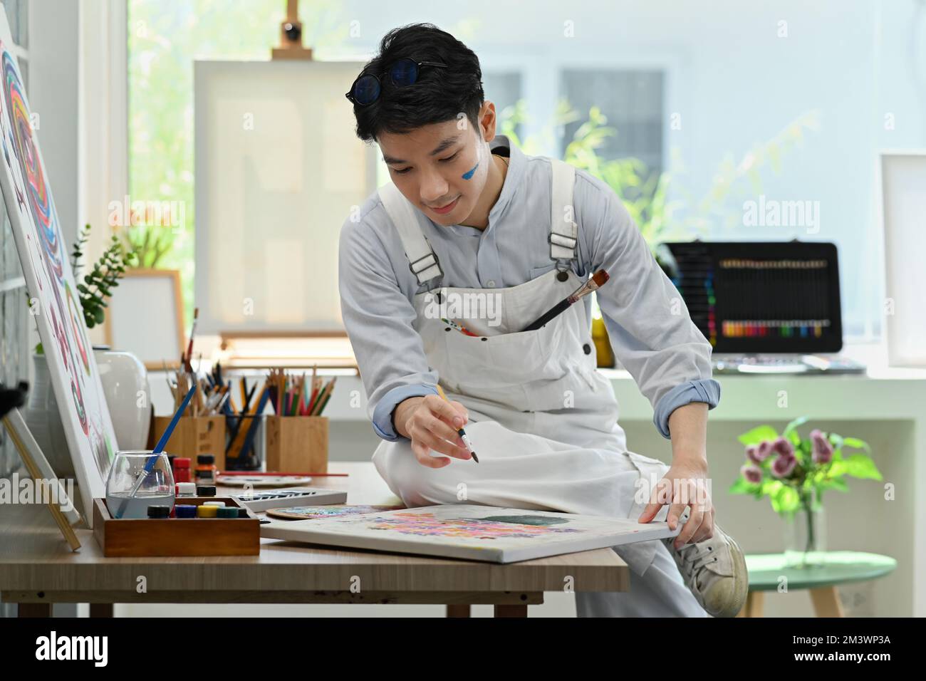 Handsome male painter creates pictures, drawing with paints on canvas ...