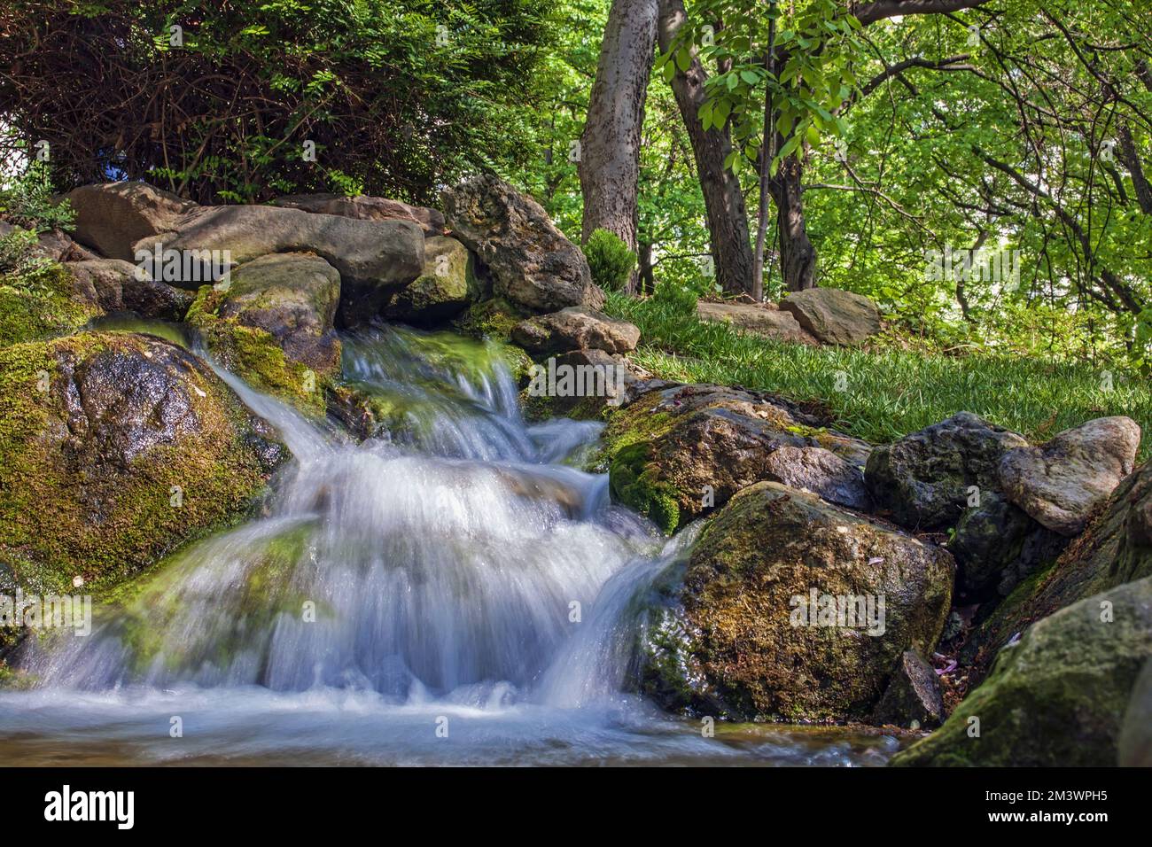 A scenic view of a small waterfall on a man-made stream in a public ...