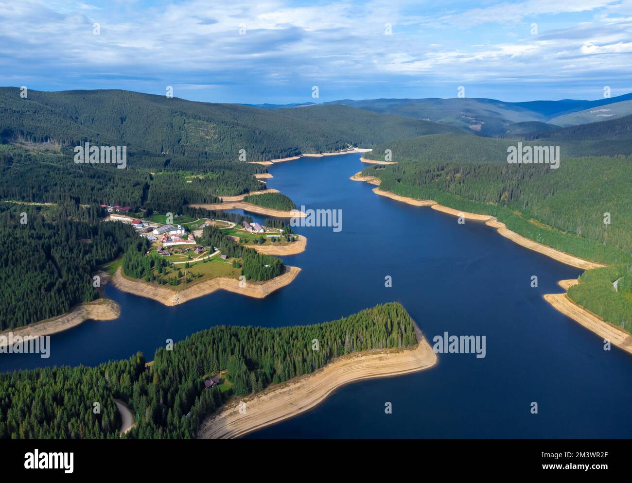 An aerial shot of Oasa lake in Romania surrounded by fir forest trees ...