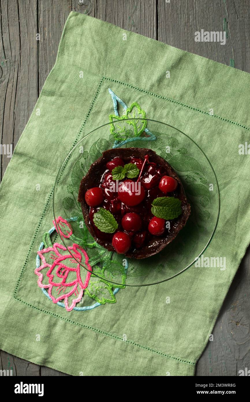 Chocolate dessert with cherries and mint on a plate on a burgundy ...