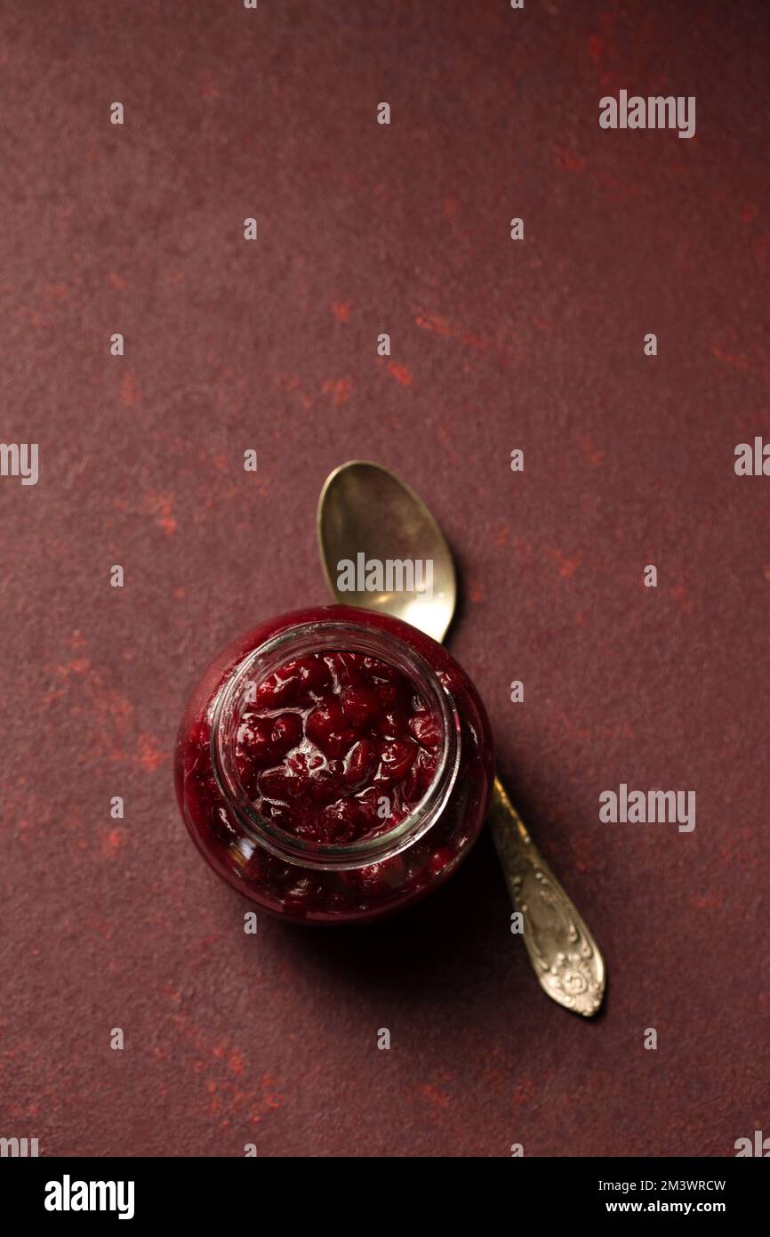 Delicious lingonberry sauce in a small glass jar on a burgundy ...