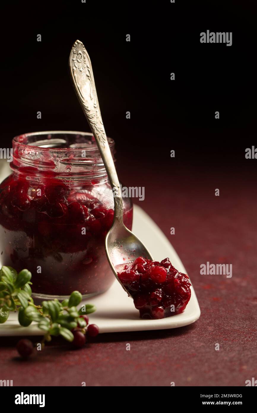 Delicious lingonberry sauce in a small glass jar on a burgundy ...