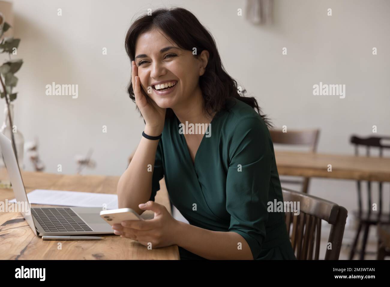 Happy freelance worker woman holding smartphone, sitting at work table ...