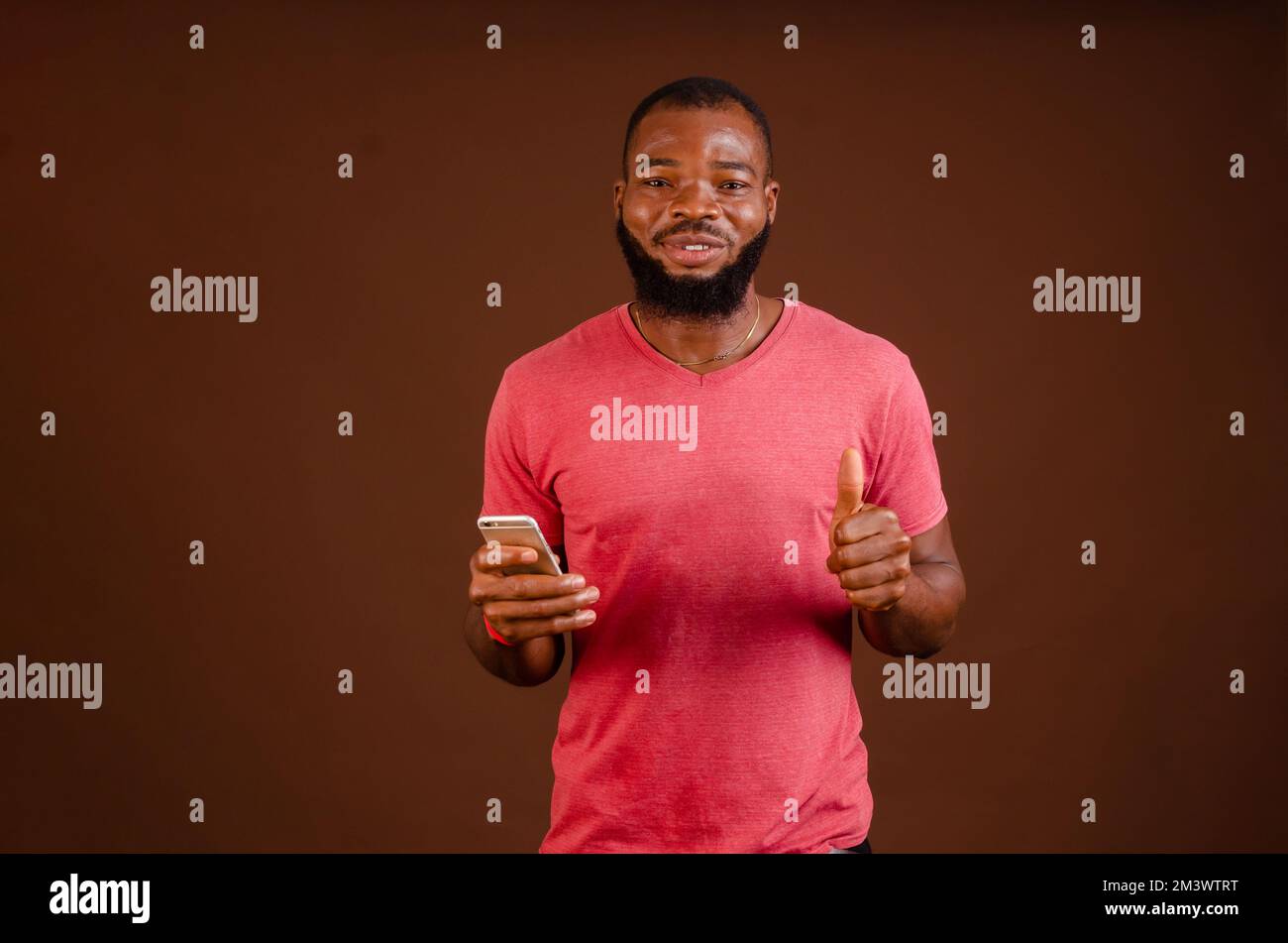 An African man holding his phone and standing in front of a brown ...