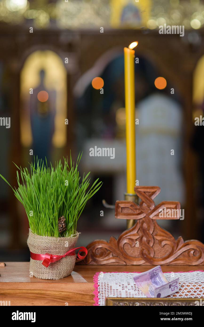 A vertical closeup of a wheatgrass, a cross, and a lit candle on the ...