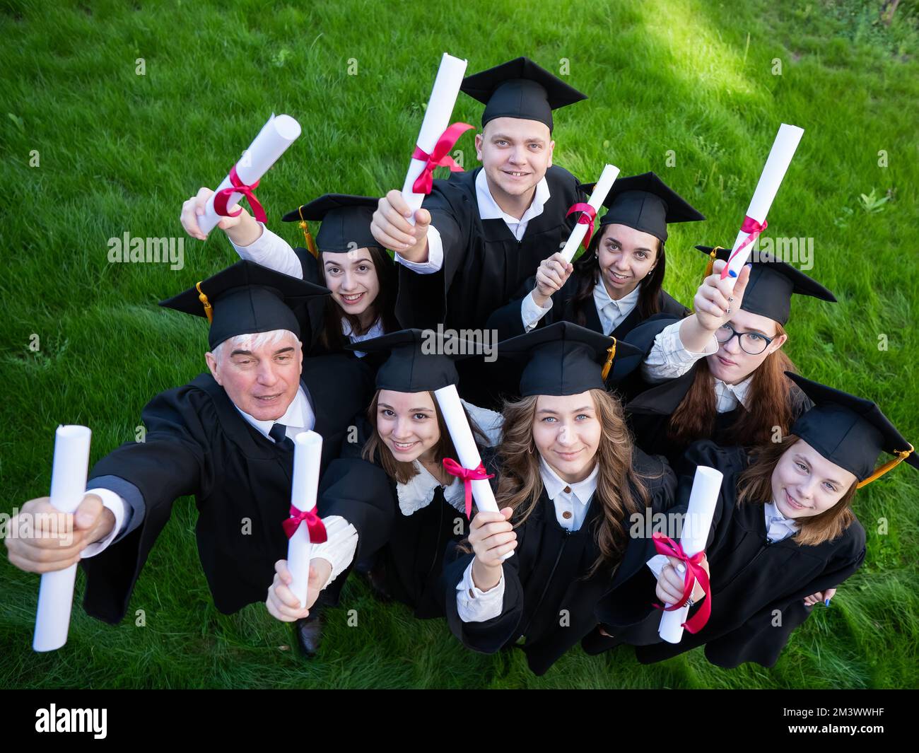 Graduates in robes show off their diplomas outdoors. View from above ...