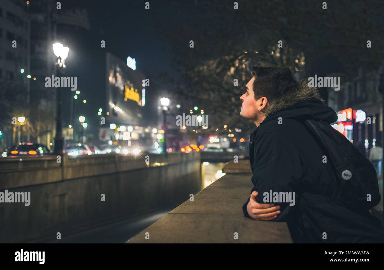 A young caucasian man leaning on a low stone wall on the street at ...