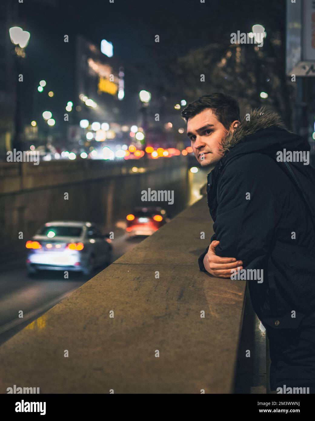 A vertical shot of a young caucasian man leaning on a low stone wall on ...