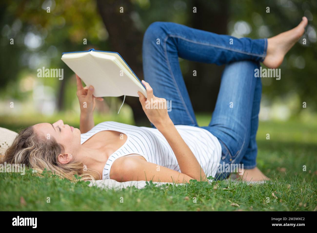 woman on her back reading a book in the park Stock Photo - Alamy