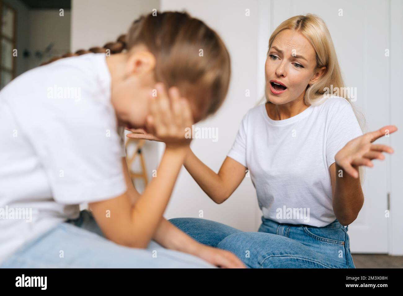 Close-up of sad depressed little girl crying covering face with palm while angry young mother ...
