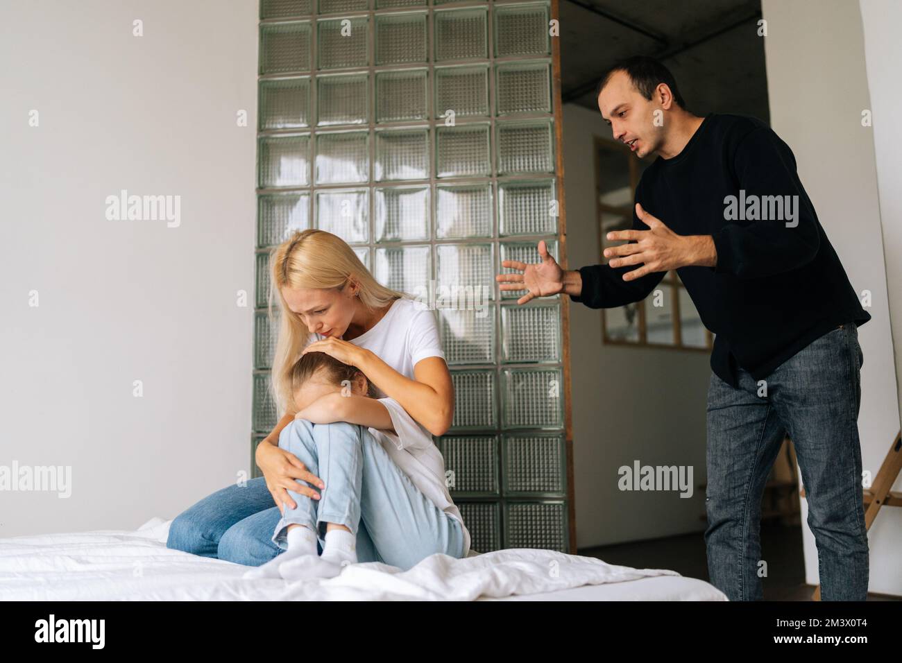 Portrait of scared mother and daughter hugging each other while father ...
