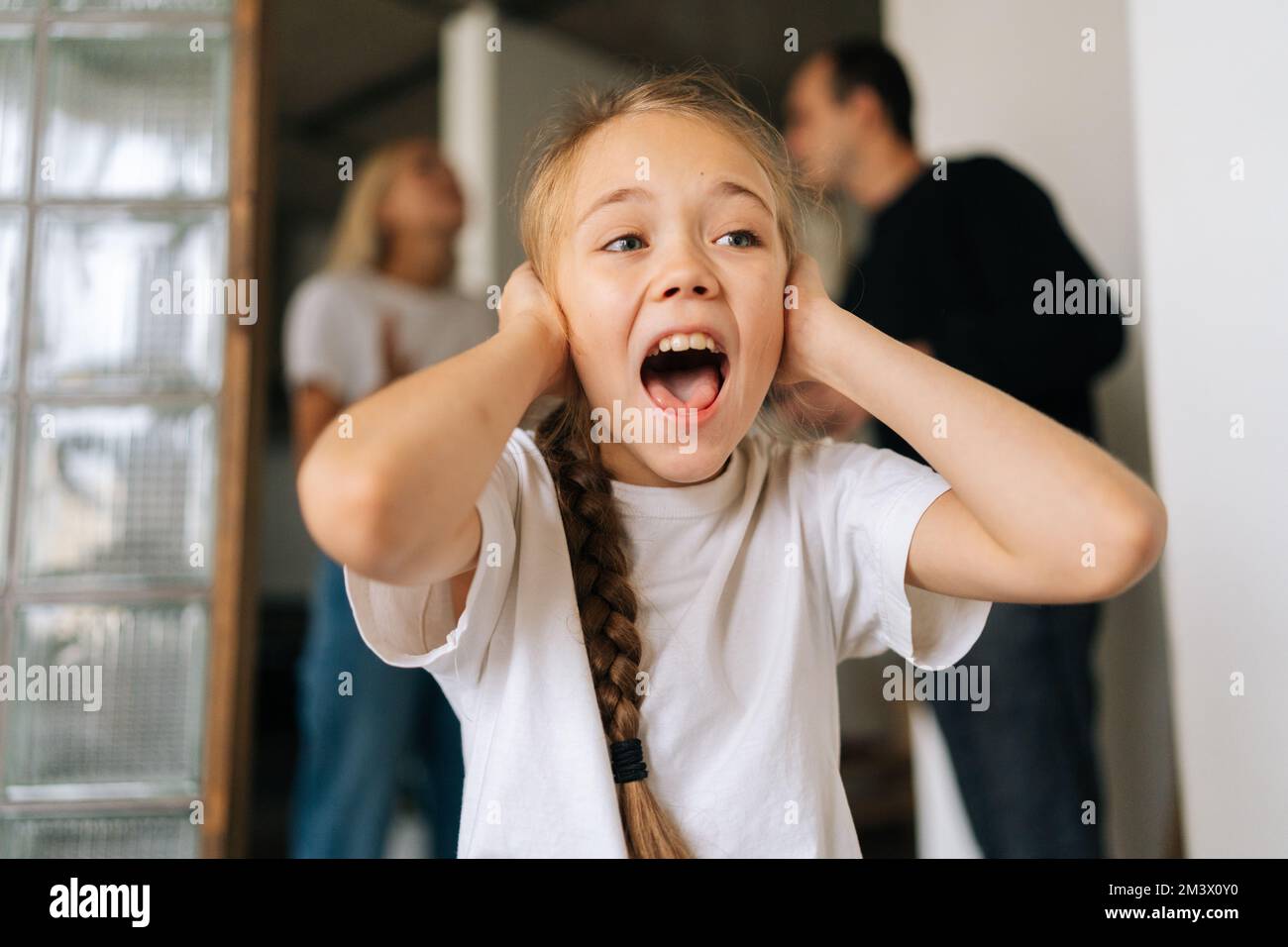Close-up portrait of excited upset little daughter screaming looking away, covering ears while ...