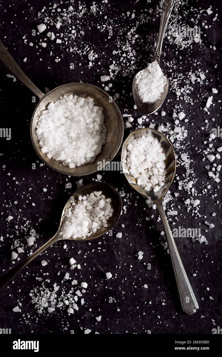 Top view of four spoons with coarse grained sea salt on black ...