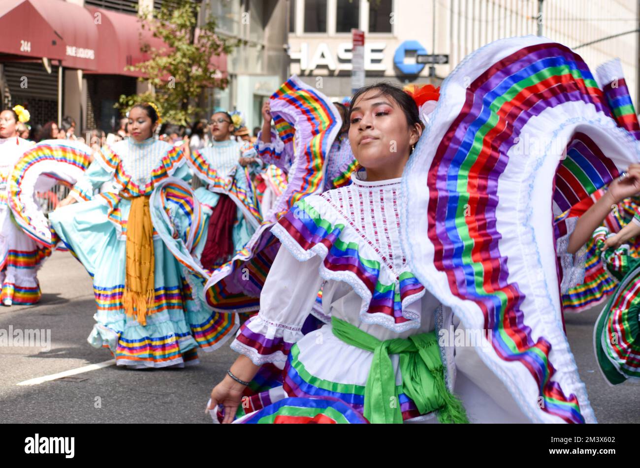 A female in a colorful dress performing on a street during the Mexican ...