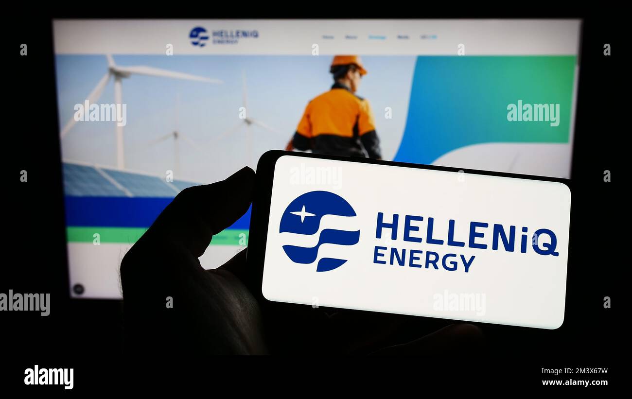 Person holding mobile phone with logo of Greek company Helleniq Energy Holdings SA on screen in ...