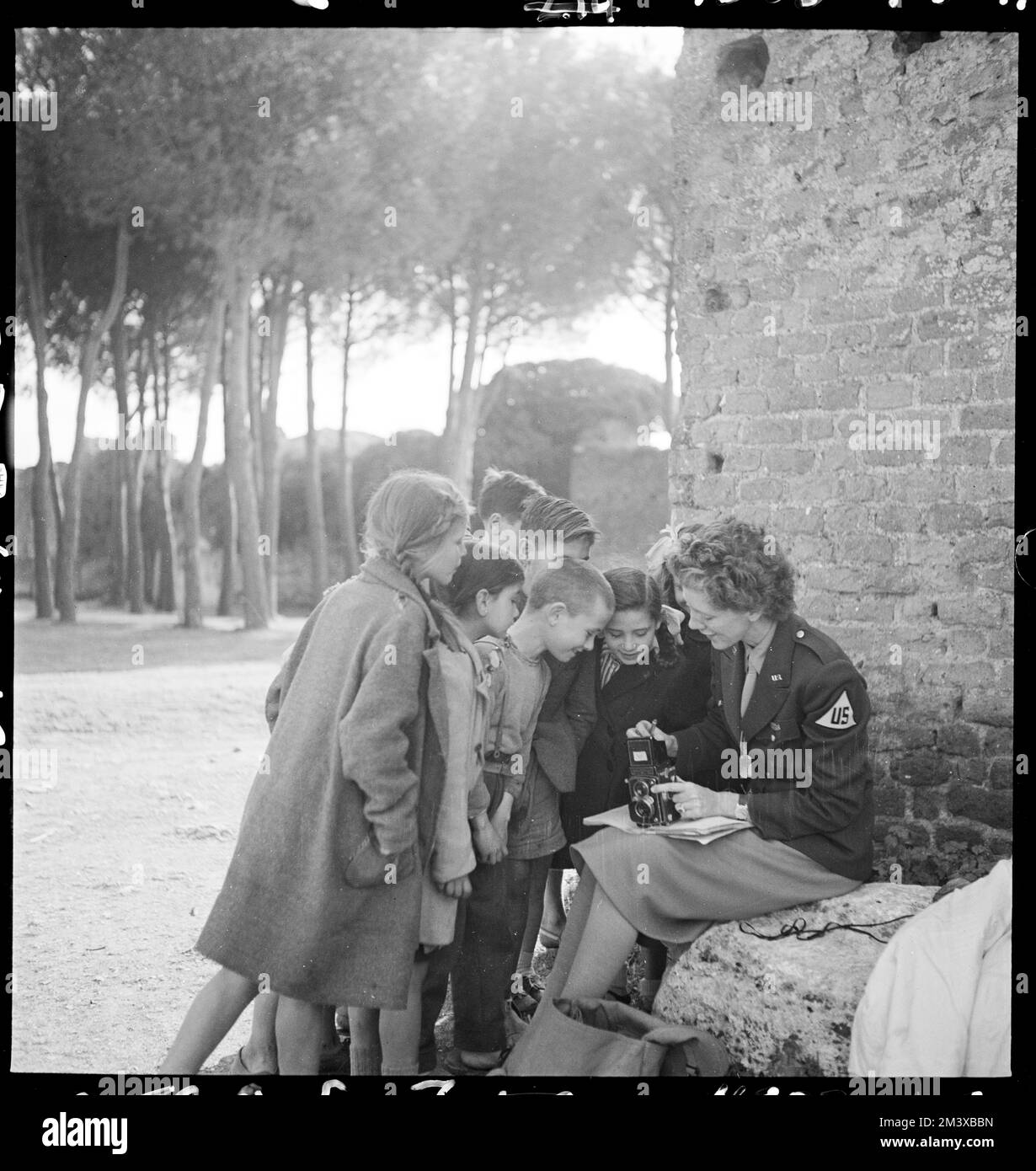 Toni Frissell, sitting, holding camera on her lap, with several ...