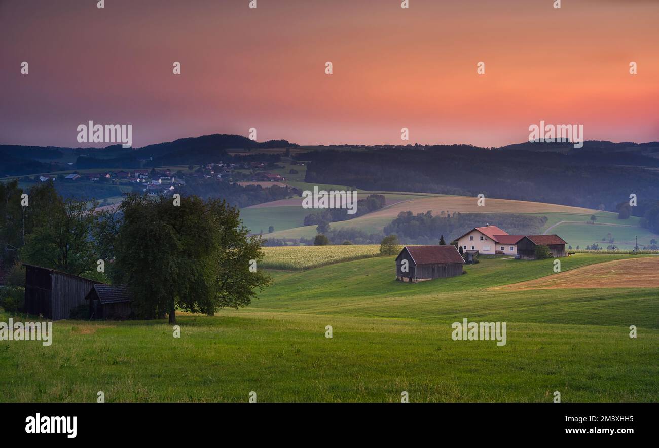A small town with a farm in front in Bavaria at sunset, surrounded by ...