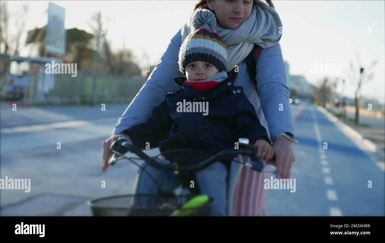 Mother rides bike with child in front during cold winter day with ...