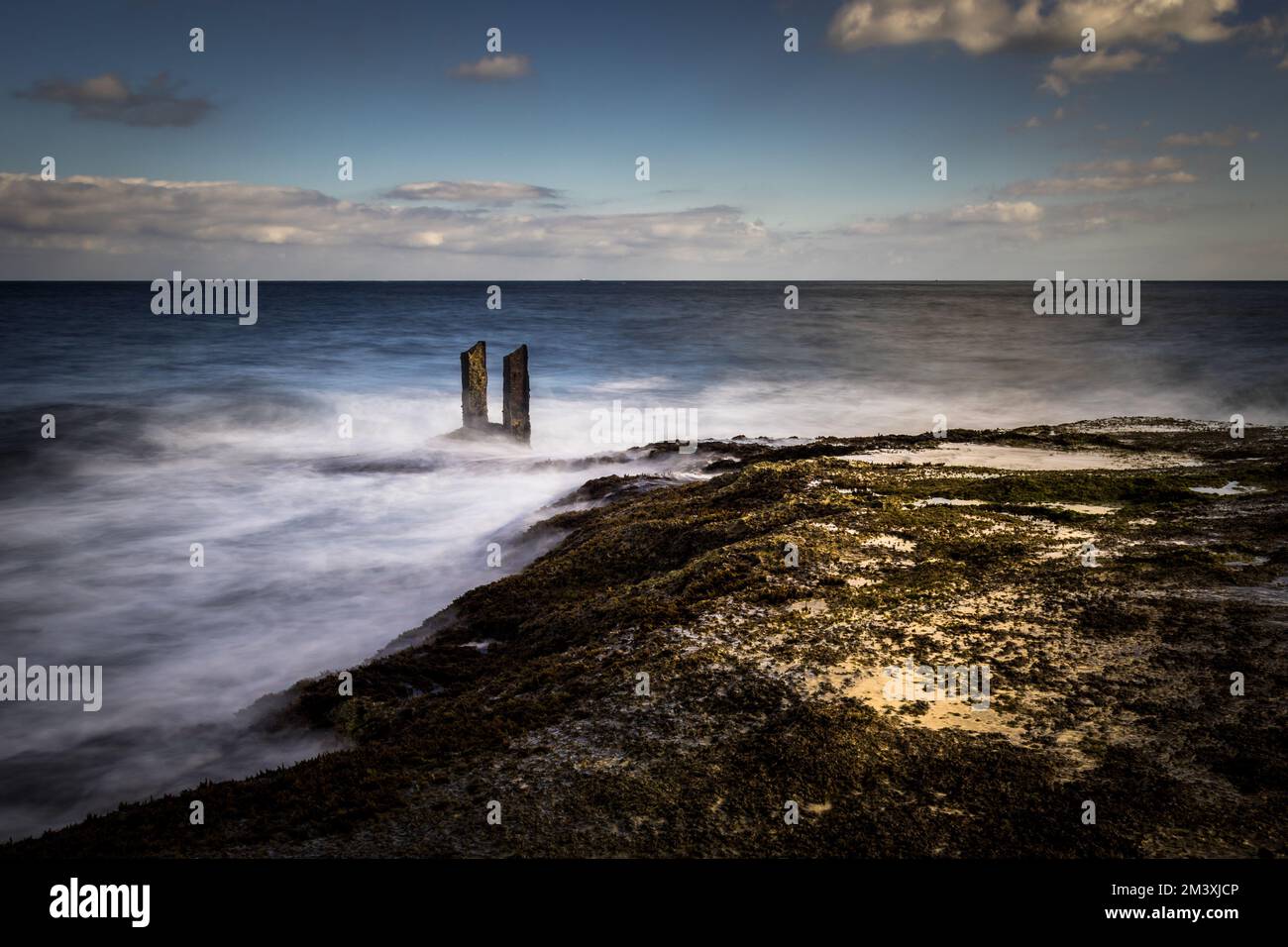 Two wooden posts sticking out of the ocean captured from the rocky ...