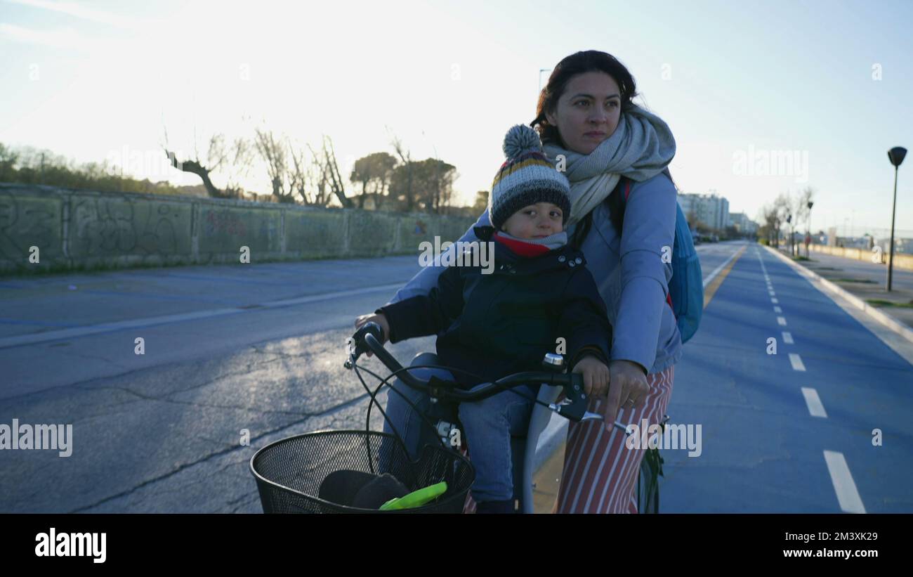 Mother rides bicycle with child in front in bike lane by sea shore ...