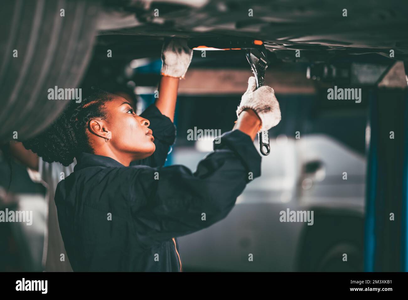 Garage women worker mechanic team working car auto service fix replace under car lift hoist ...