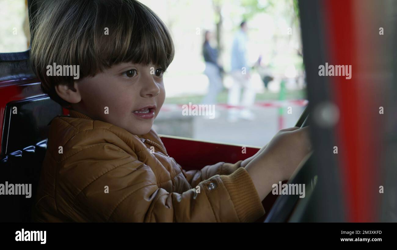 One happy small boy driving toy car interior at amusement park carousel ...