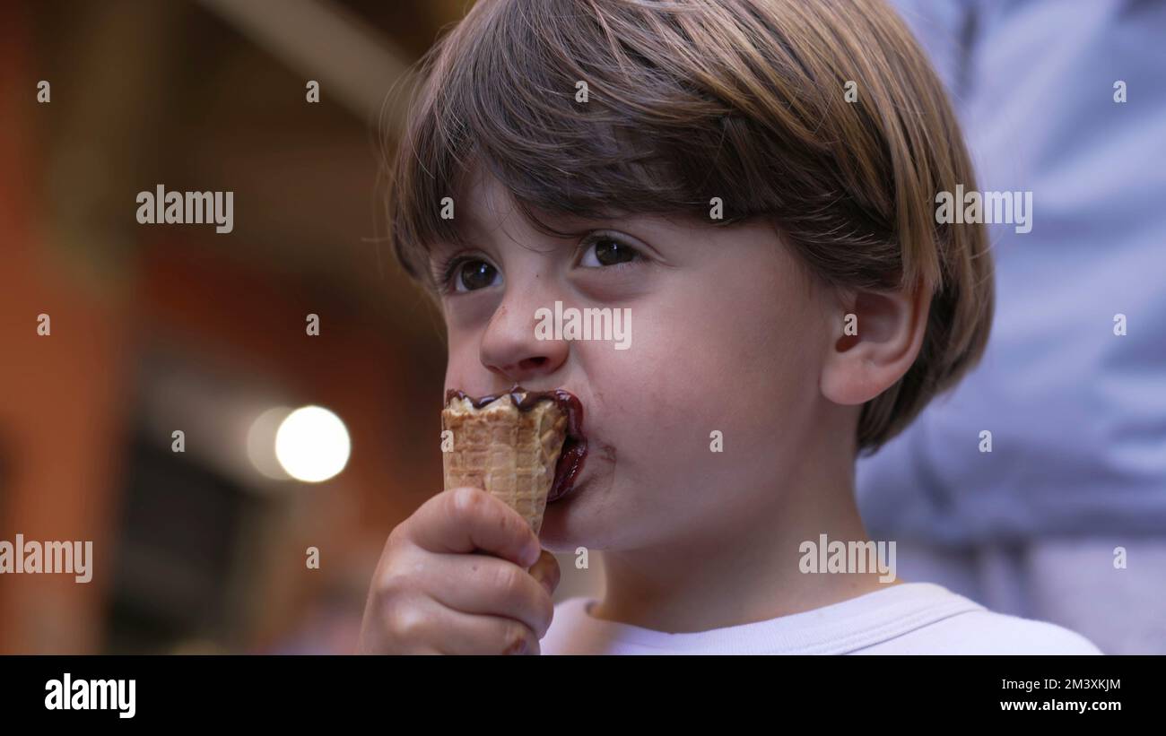 Small boy enjoying ice cream dessert outside in street. Portrait face ...