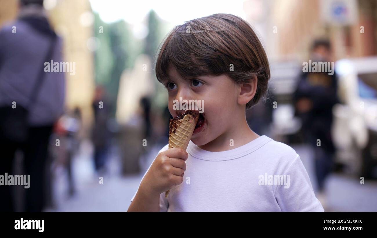 Young boy eating ice cream cone outside. Child eats italian gelato ...
