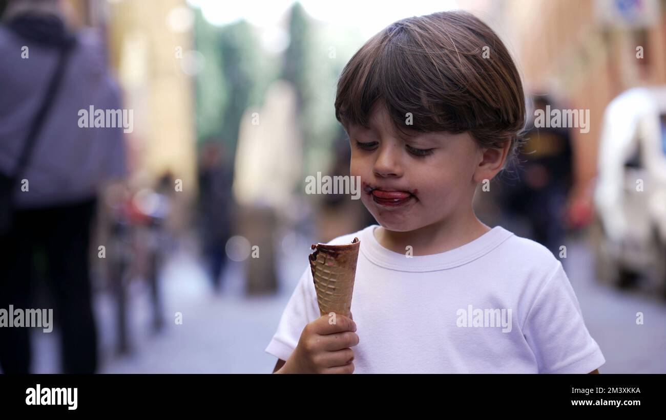Young boy eating ice cream cone outside. Child eats italian gelato ...