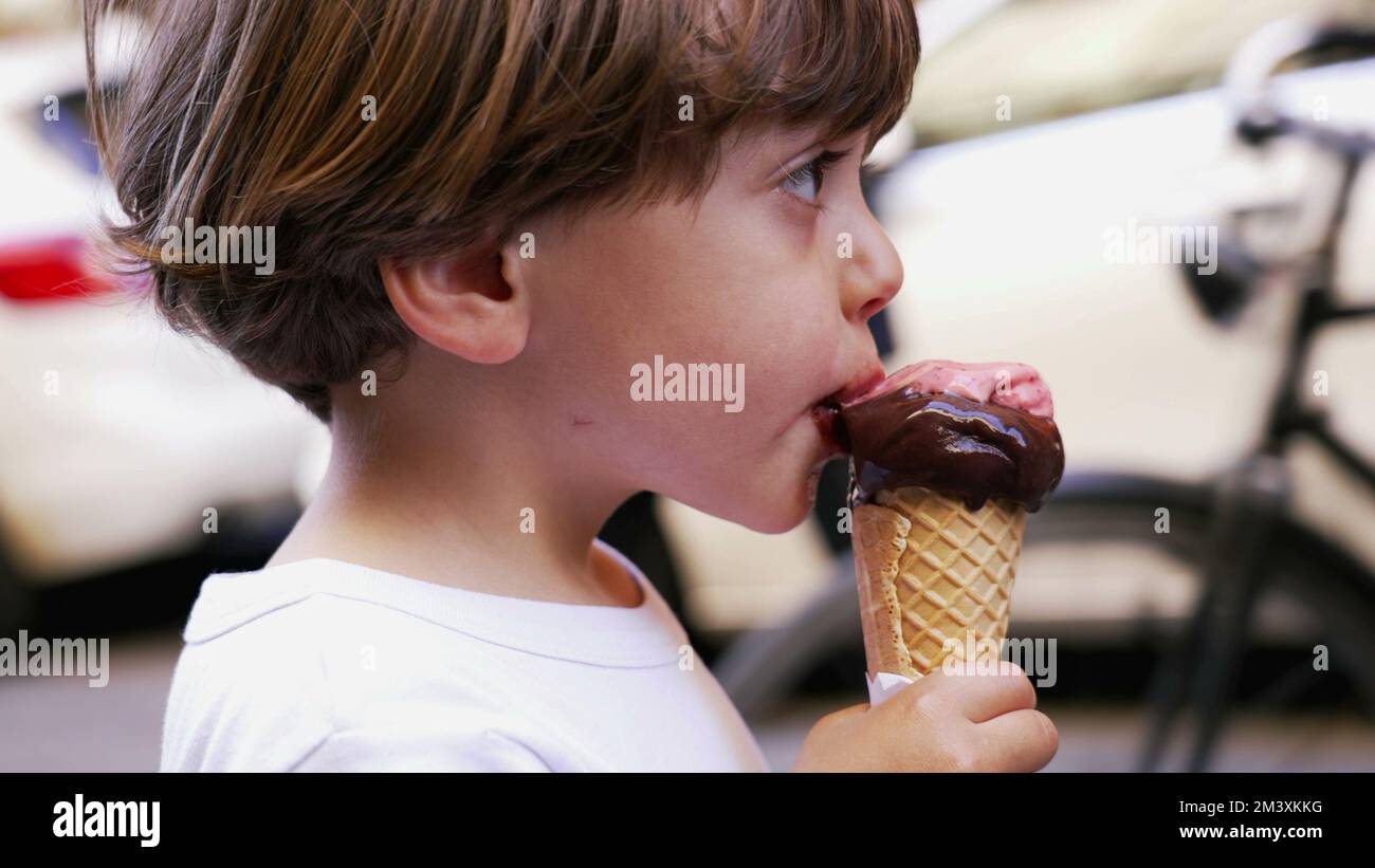 Young boy eating ice cream cone outside. Child eats italian gelato ...