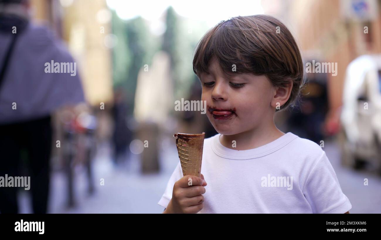Young boy eating ice cream cone outside. Child eats italian gelato ...