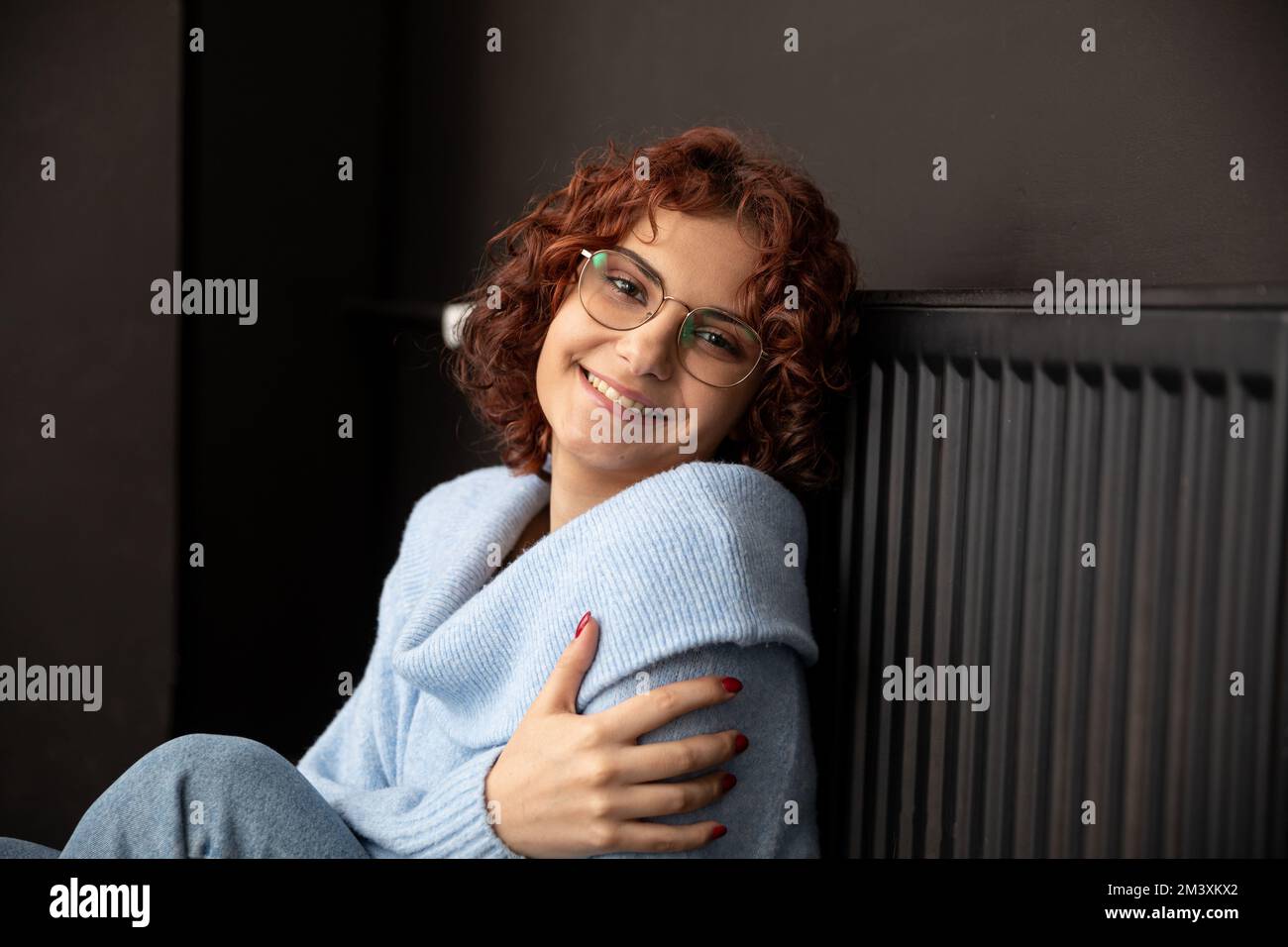 A smiling girl sits and leans against a hot radiator Stock Photo - Alamy