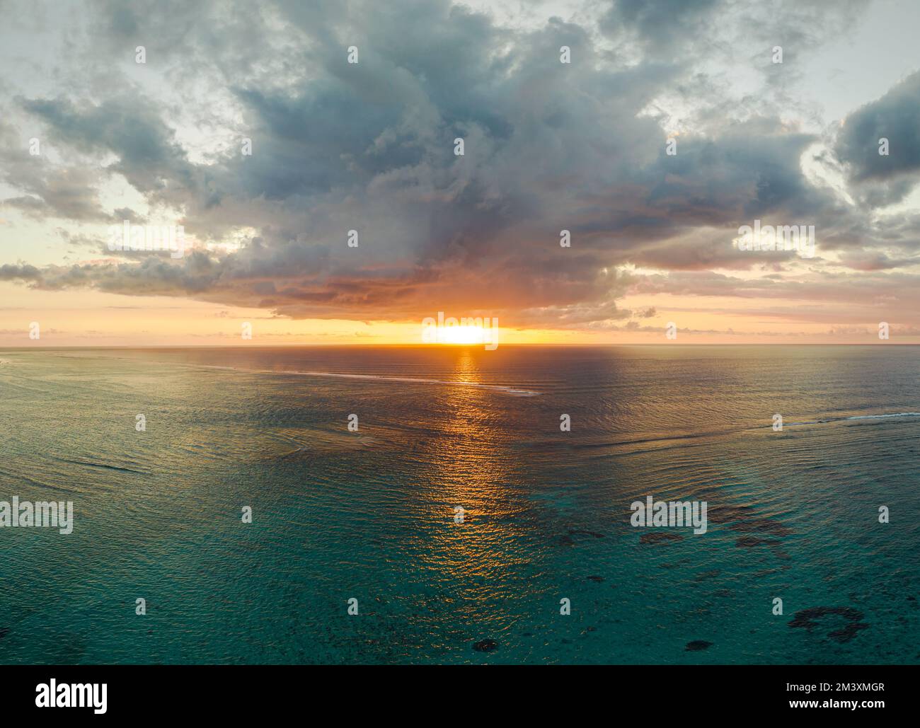 Sun is shining between the clouds and ocean at sunset time. The ...