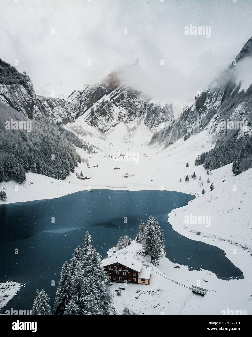 A vertical shot of a lake surrounded by rocky hills covered in the snow ...